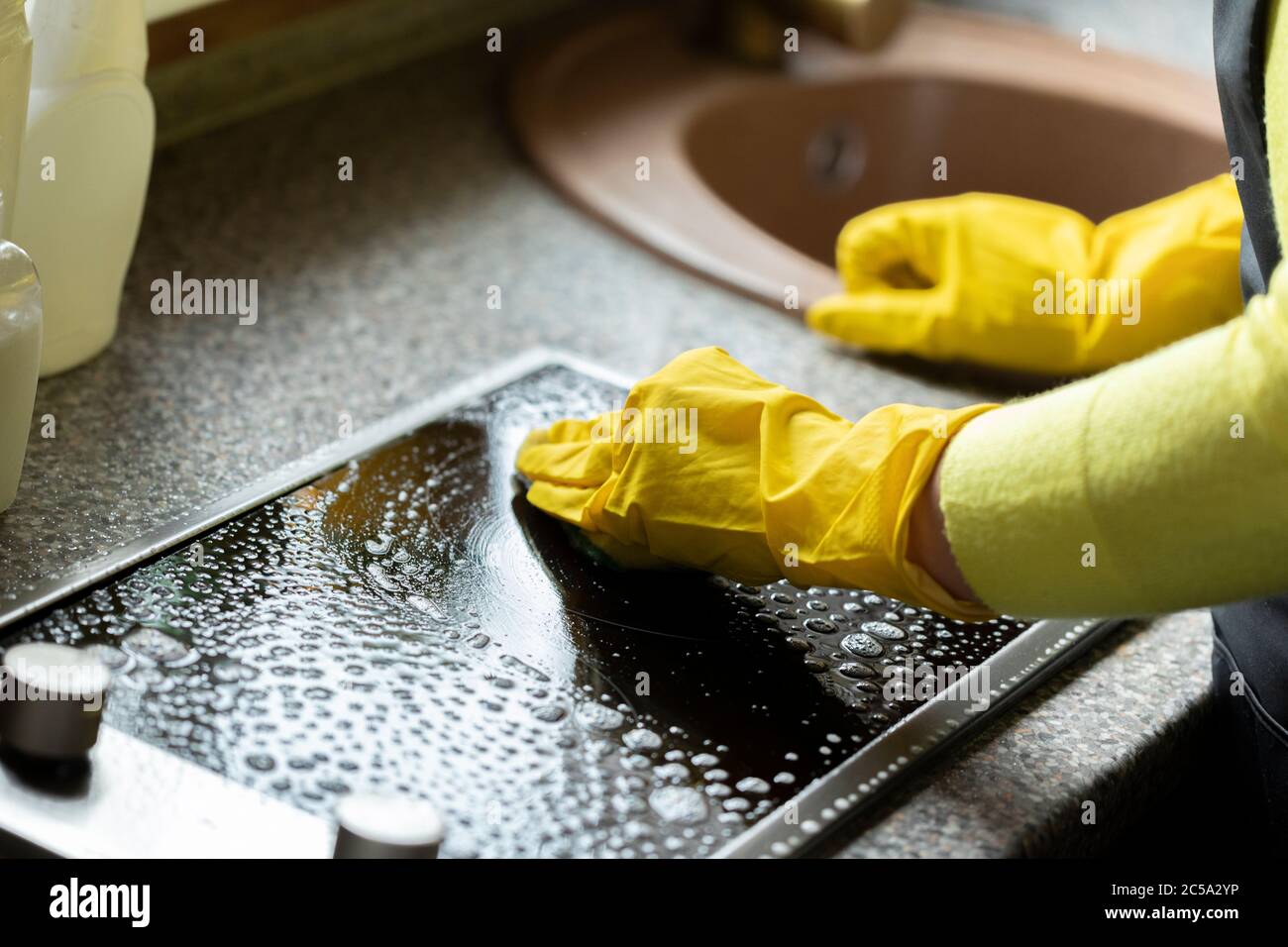 Hands in yellow gloves wipe surface of black induction stove close up ...