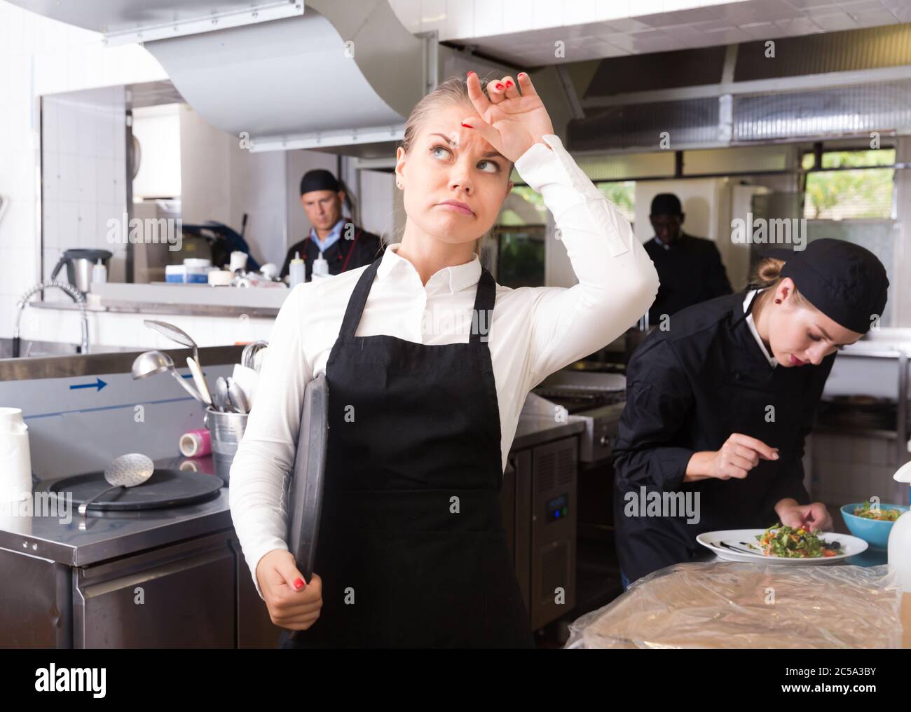 Unhappy and tired young waitress waiting ordered dishes in restaurant ...