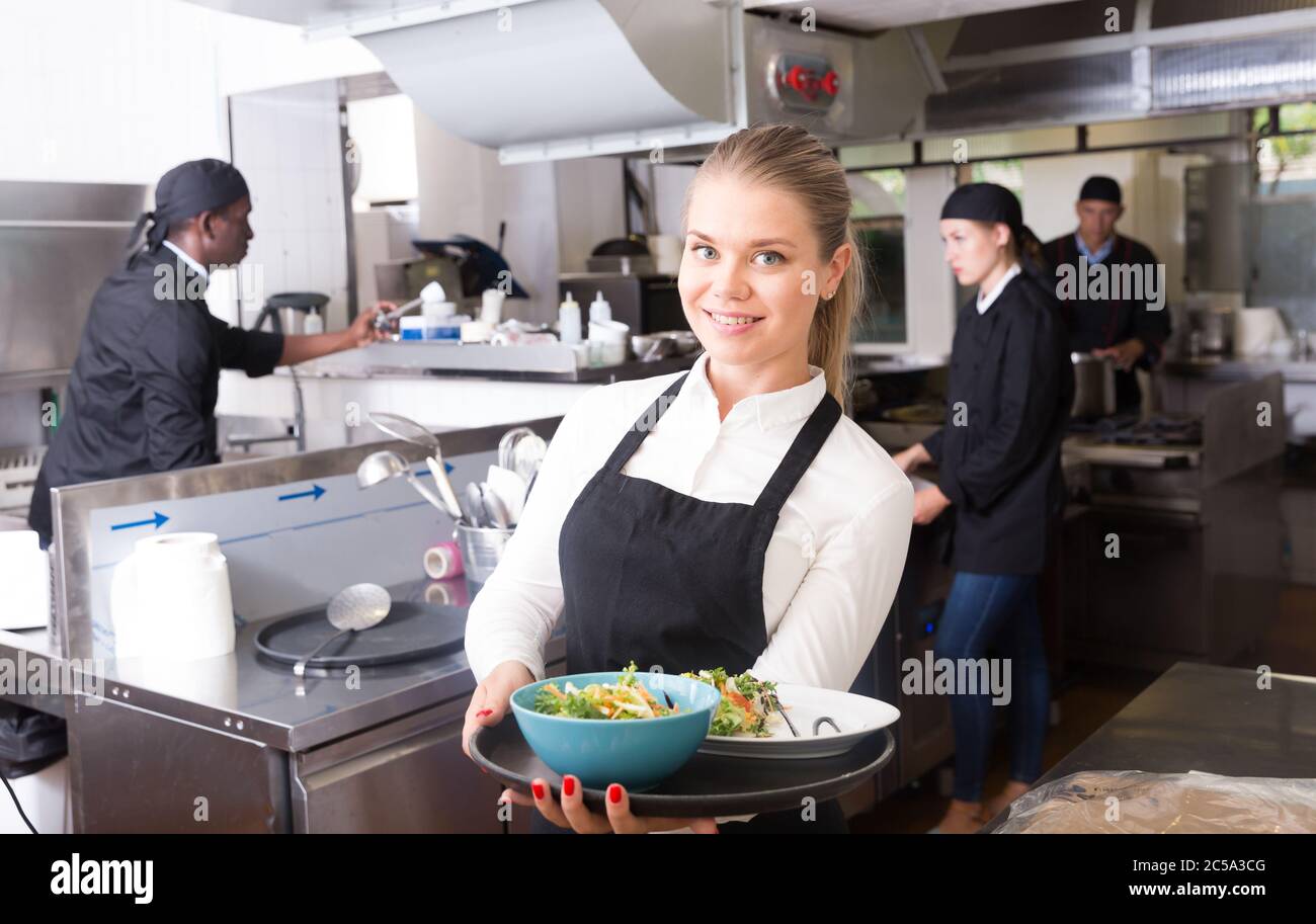 Successful young waitress standing in restaurant kitchen with ordered ...