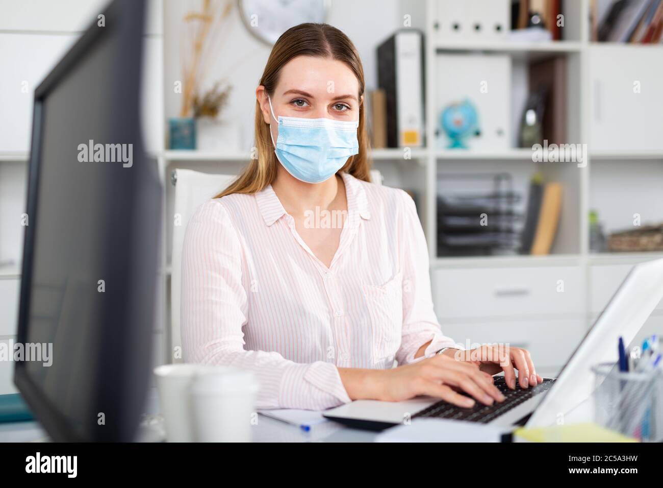 Young female worker wearing medical facial mask engaged in business ...