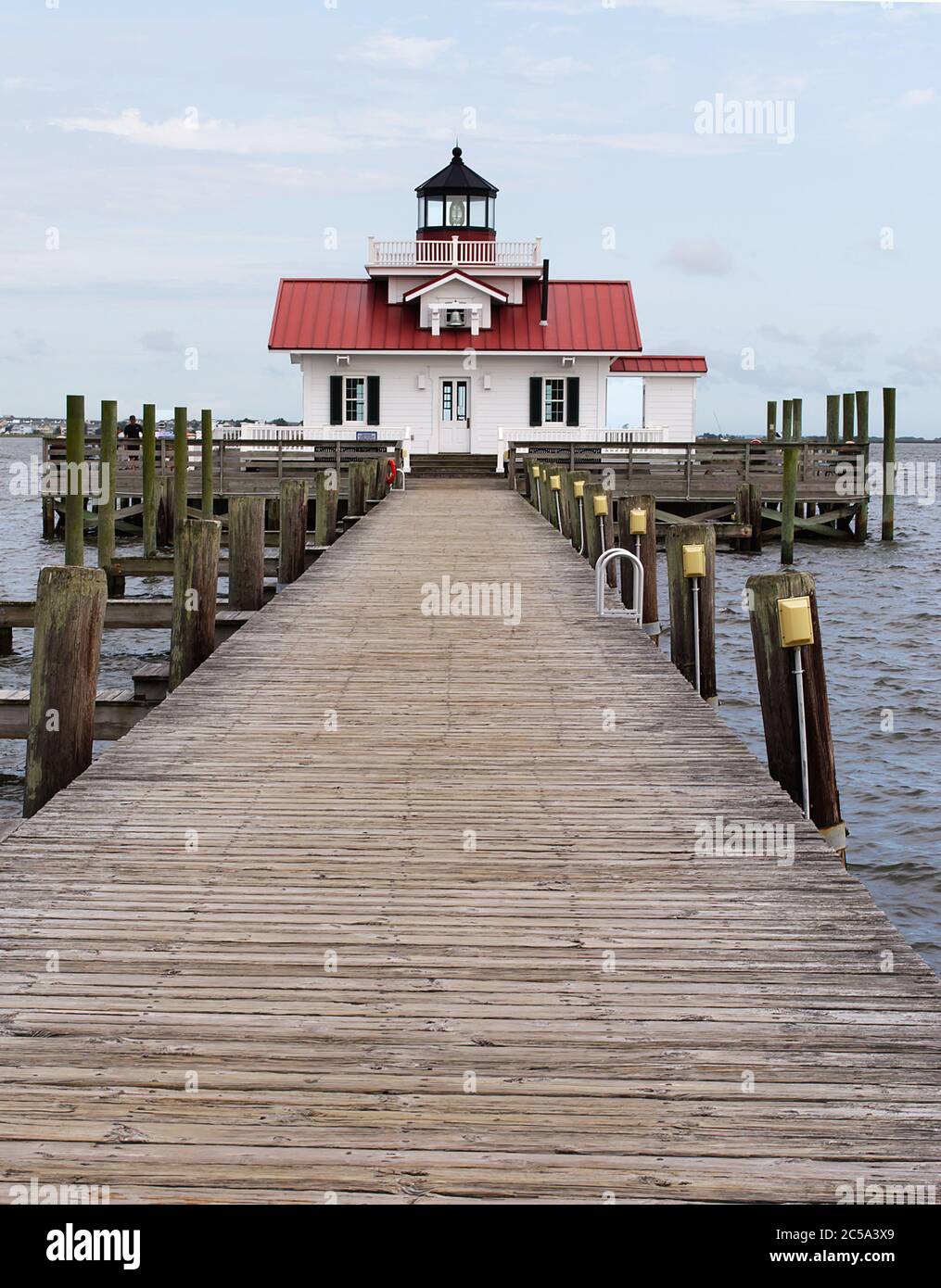 A small lighthouse at the end of a pier with a red roof and white ...
