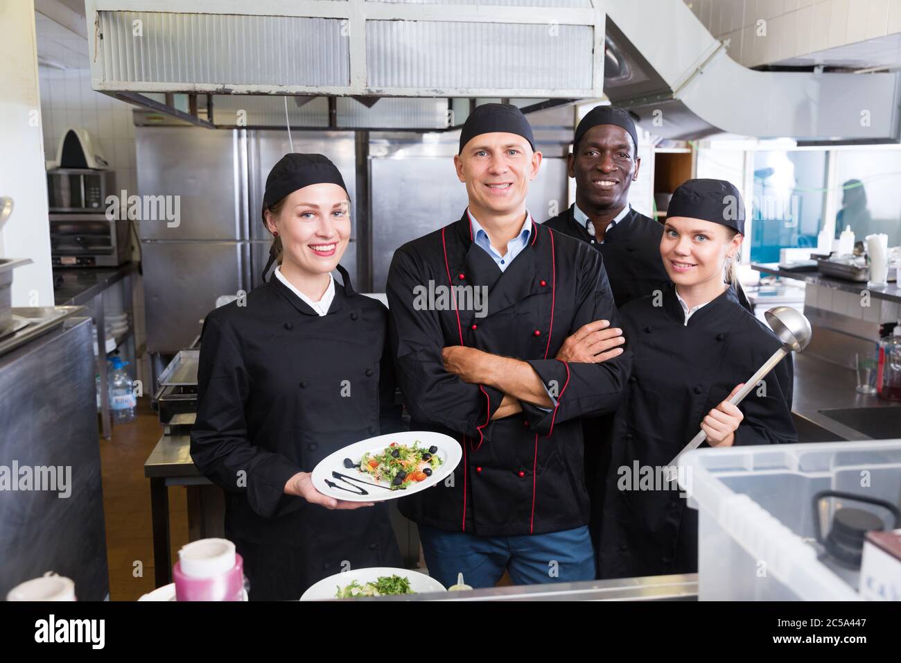 Group portrait of professional chefs posing together in modern kitchen ...