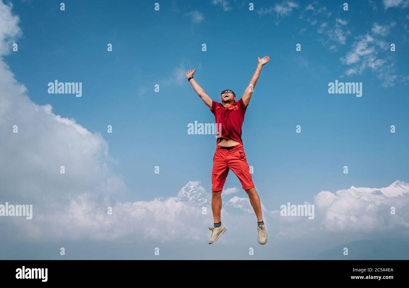Happy man dressed red jumping over the clouds with Annapurna range ...