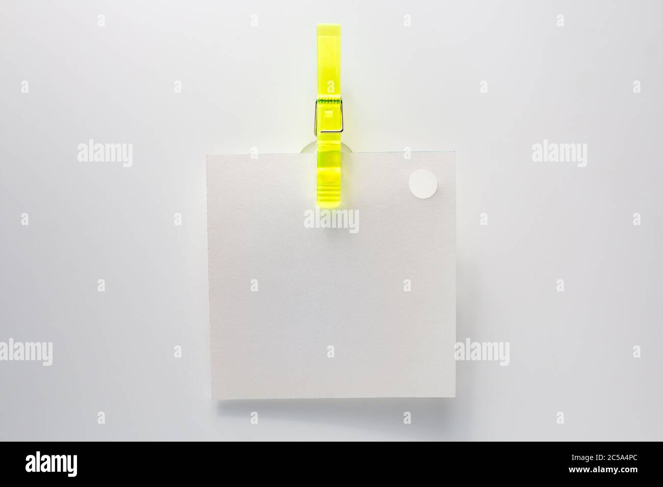 A blank note hanging on a white wall with a yellow clip. Office Stock ...