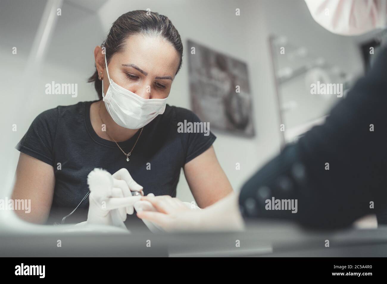 Professional manicure master dressed black in safety face mask using ...