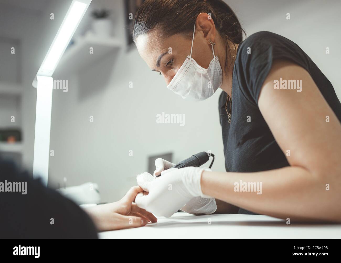 Professional manicure master dressed black in safety face mask using ...