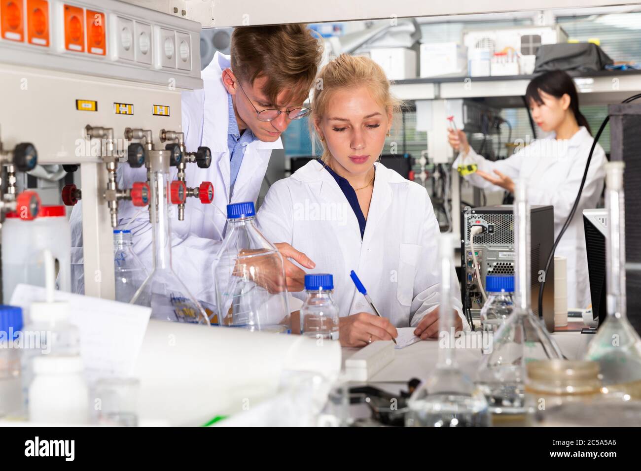 Young Caucasian and Asian students engaged in research at chemical lab ...
