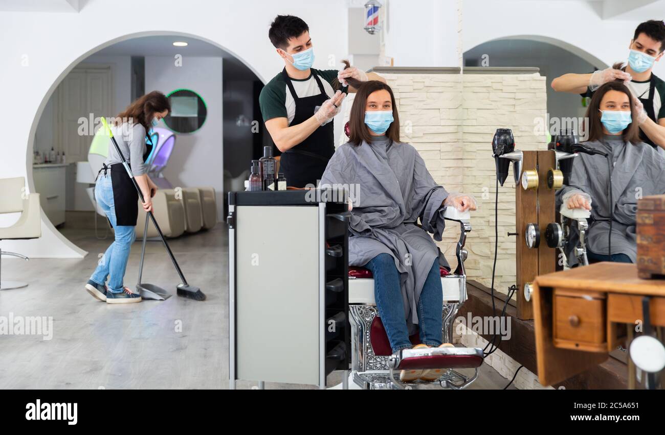 Young male hairdresser in mask cuts hair of girl in mask at beauty ...