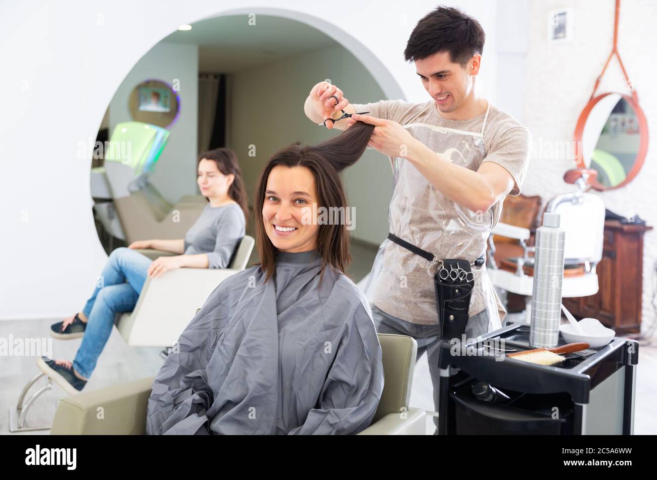 Young man stylist working in beauty studio doing haircut and hair ...