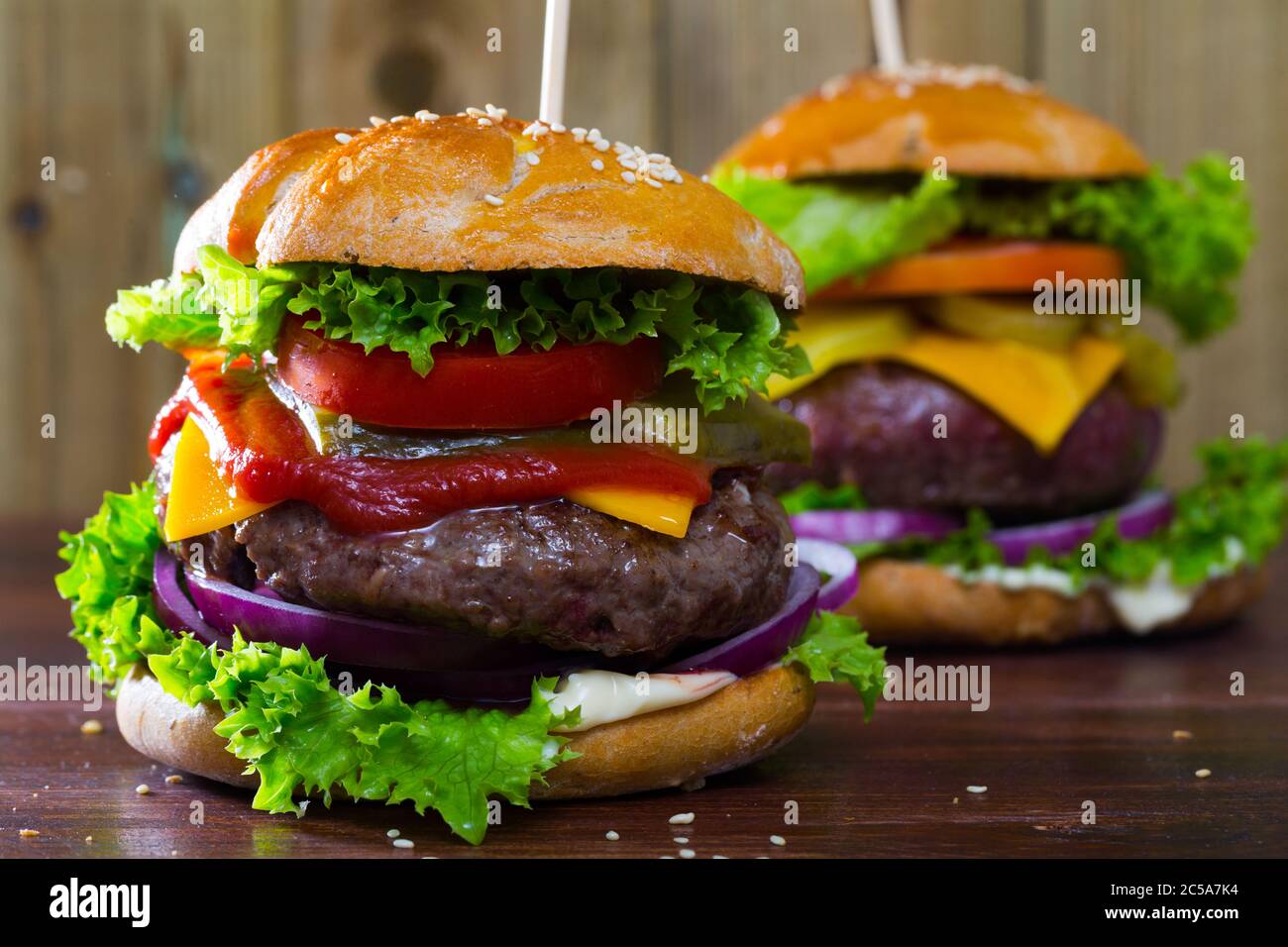 Two delicious burgers with cheese, tomato, pickled cucumbers, onion and ...
