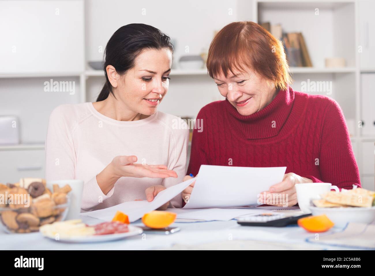 Happy women with documents sitting at table in home interior Stock ...