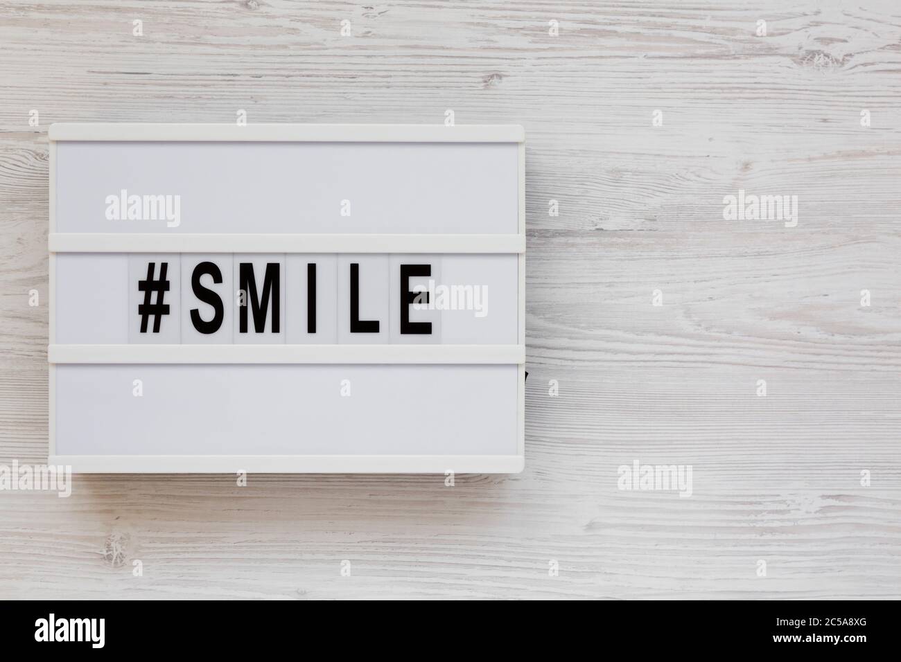 'Smile' word on a lightbox on a white wooden background, top view. Flat ...
