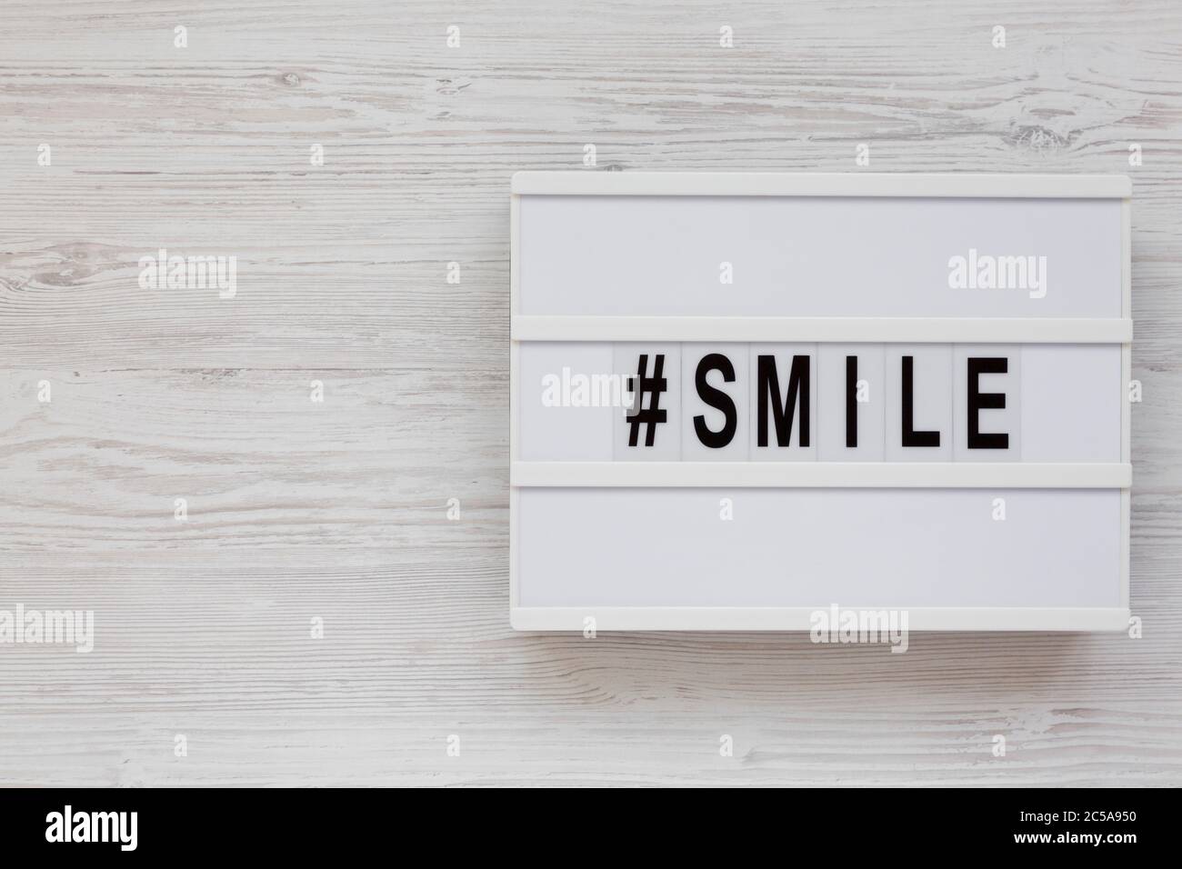 'Smile' word on a lightbox on a white wooden background, top view. Flat ...