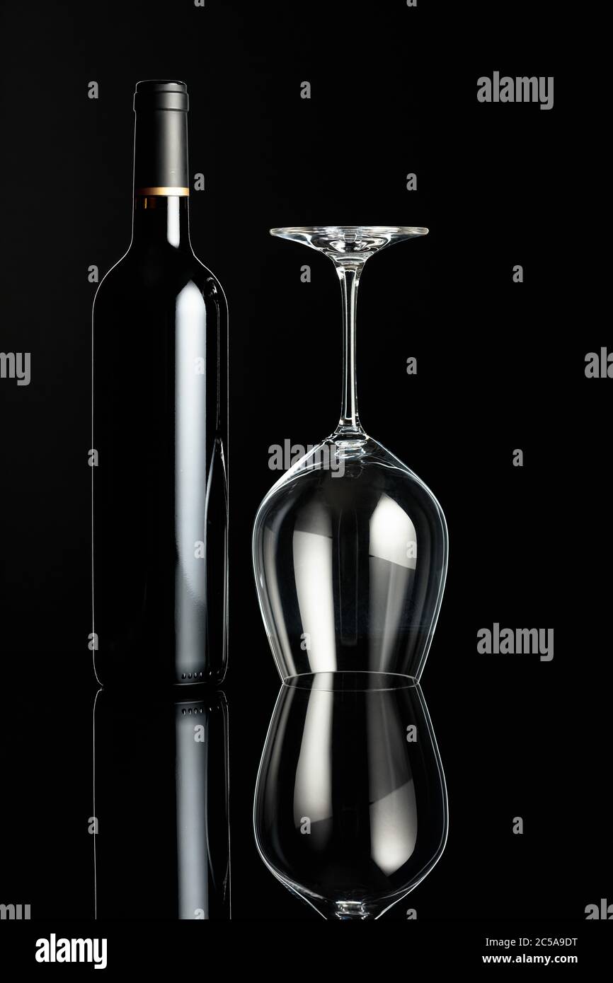 Bottle of red wine and an inverted wine glass on a black background ...