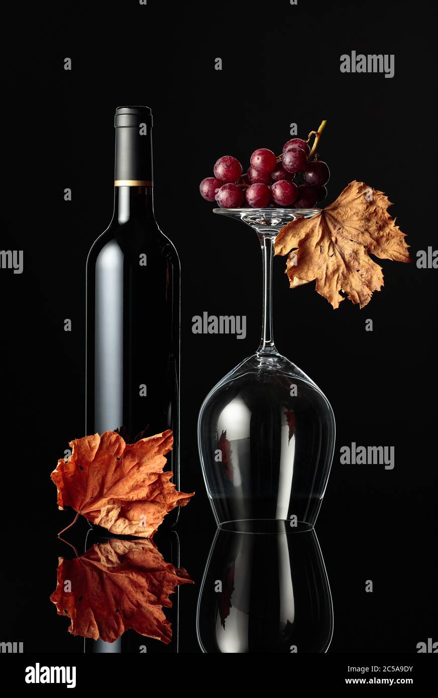 Bottle of red wine and an inverted wine glass on a black background ...