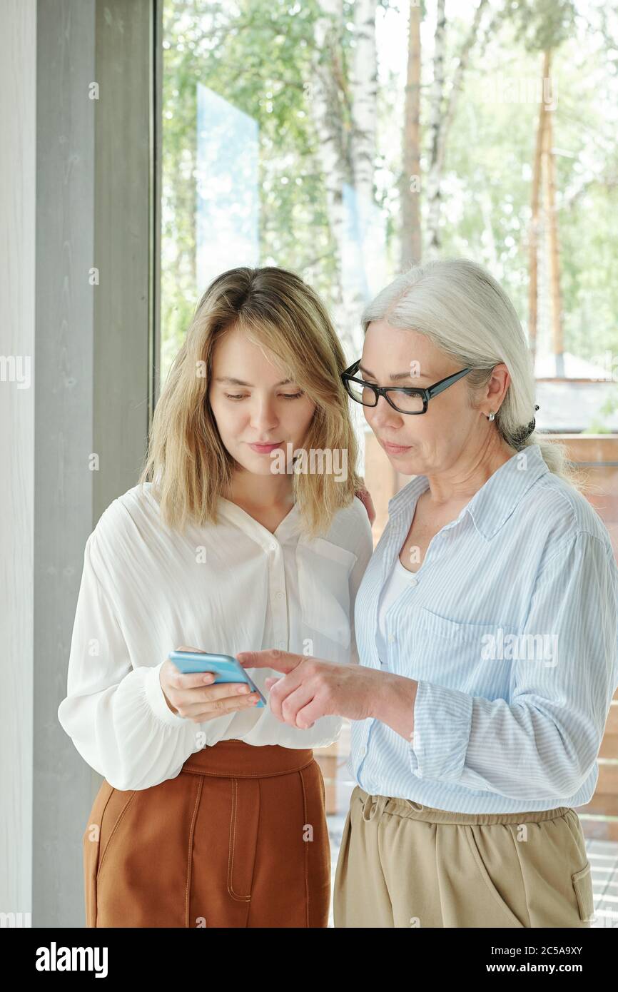 Young blond-haired woman showing phone app to senior mother while ...