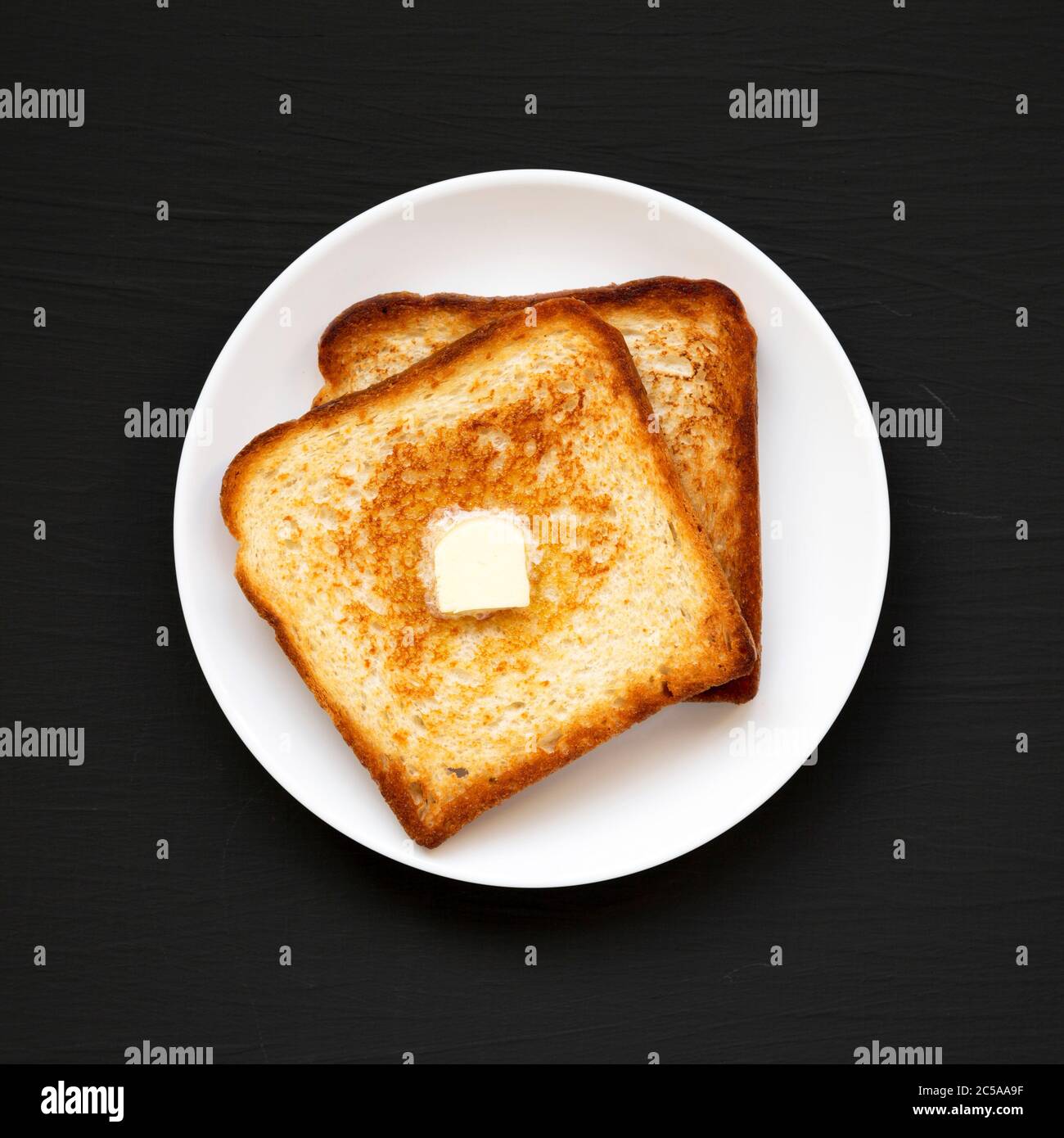 Homemade Buttered Toast on a white plate on a black surface, top view ...
