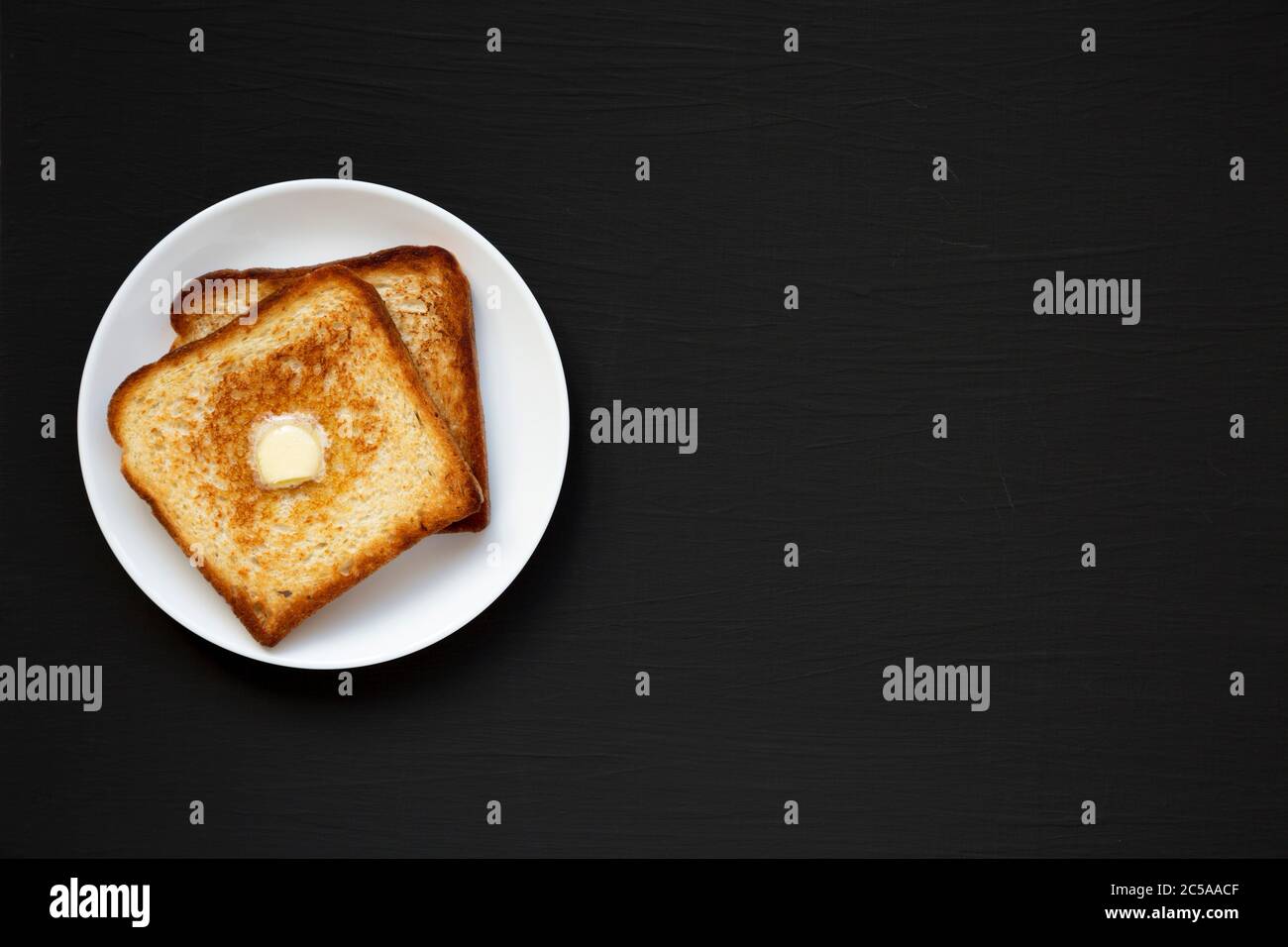 Homemade Buttered Toast on a white plate on a black surface, top view ...