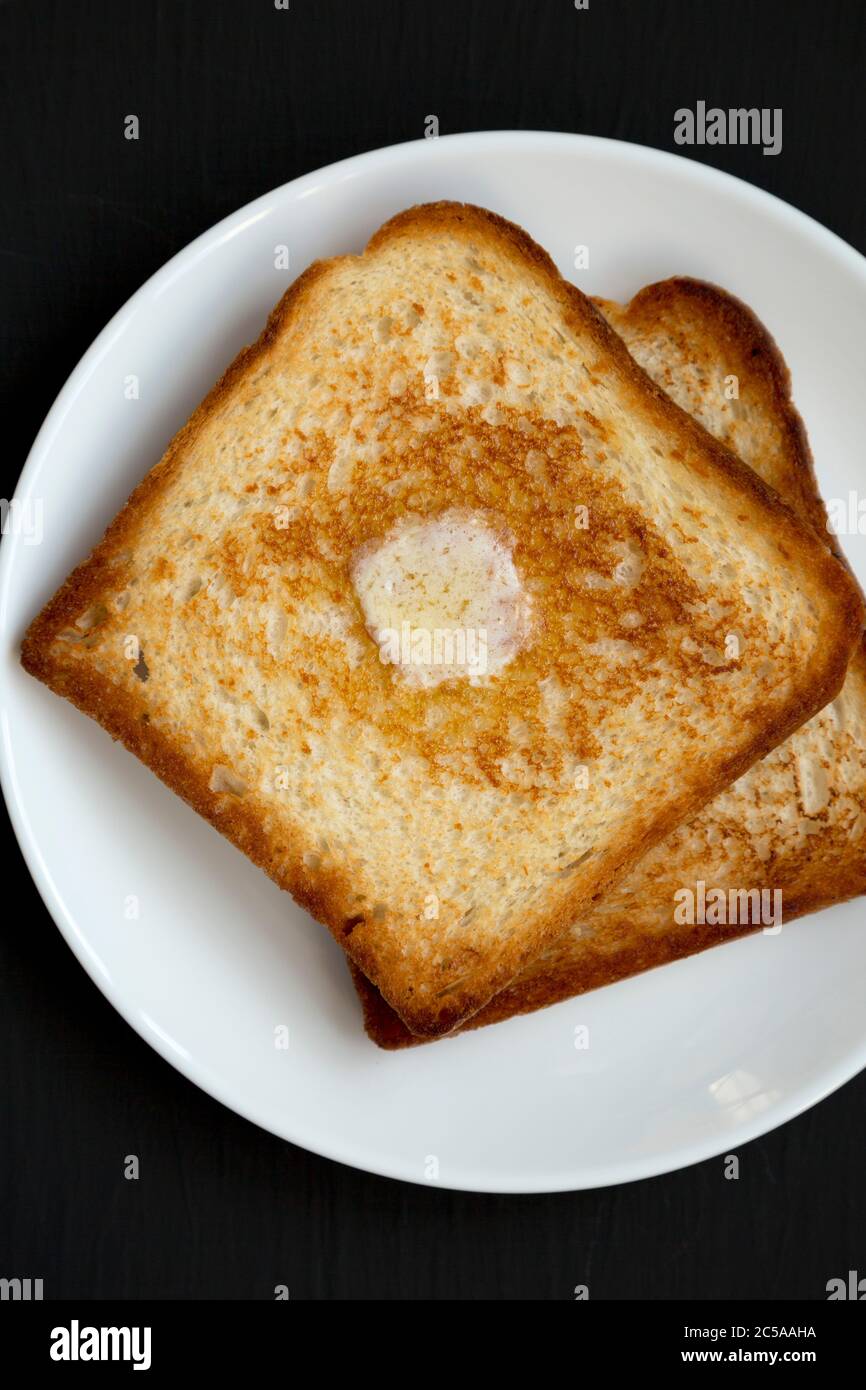 Homemade Buttered Toast on a white plate on a black background, top ...