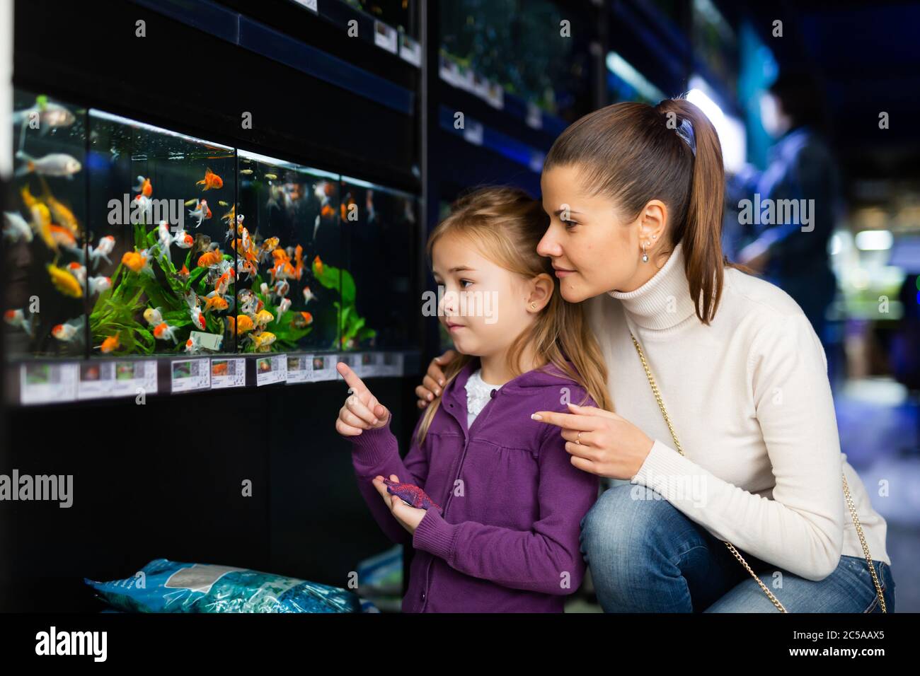 Happy little girl with mother choosing new aquarium fish for home fish ...