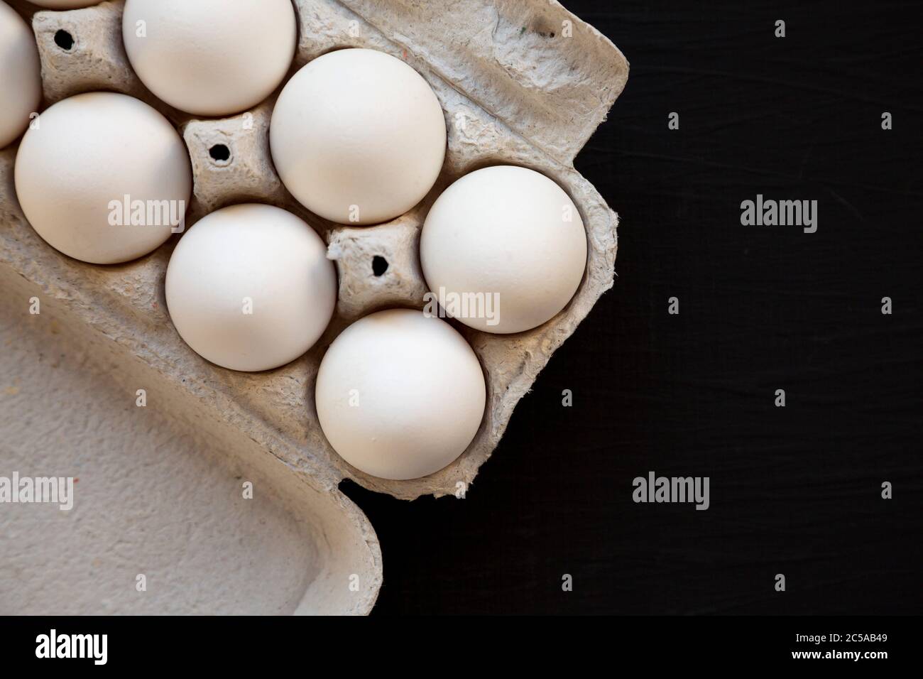 Uncooked Organic White Eggs in a paper box on a black surface, top view ...