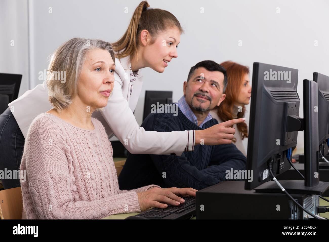 Computer lessons for adults. Young female tutor explaining to mature ...