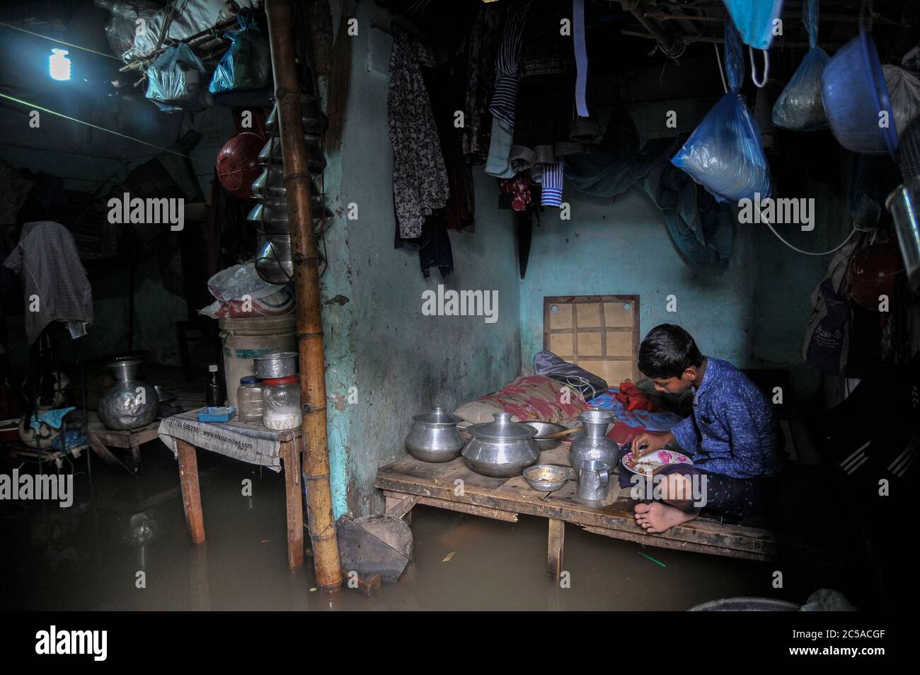 A boy eating on top of a bed amidst flood water in a slum in kamalgor ...