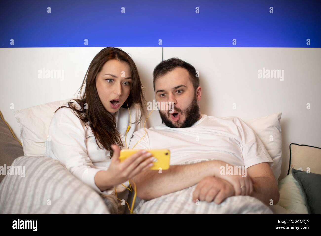 Shocked and scared couple watching horror movies on smartphone lying in ...