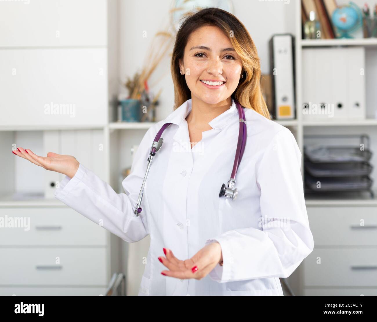 Portrait of young latina female doctor making welcome gesture welcoming ...