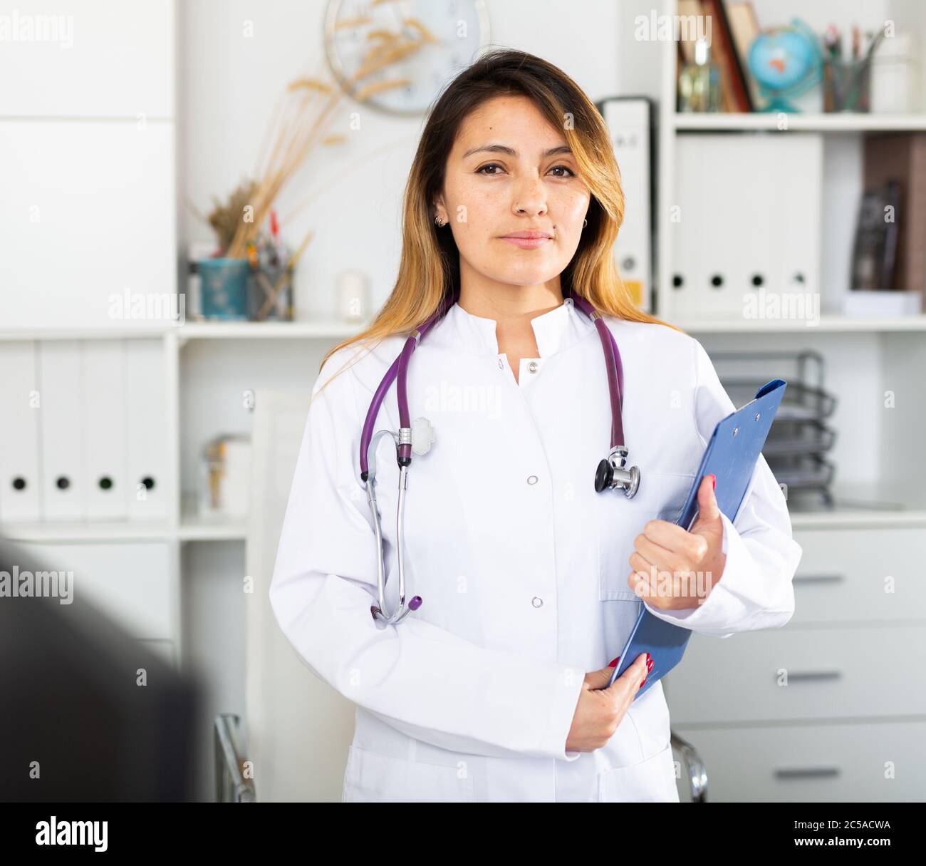 Young mexican female medic in uniform holding clipboard in doctor's ...