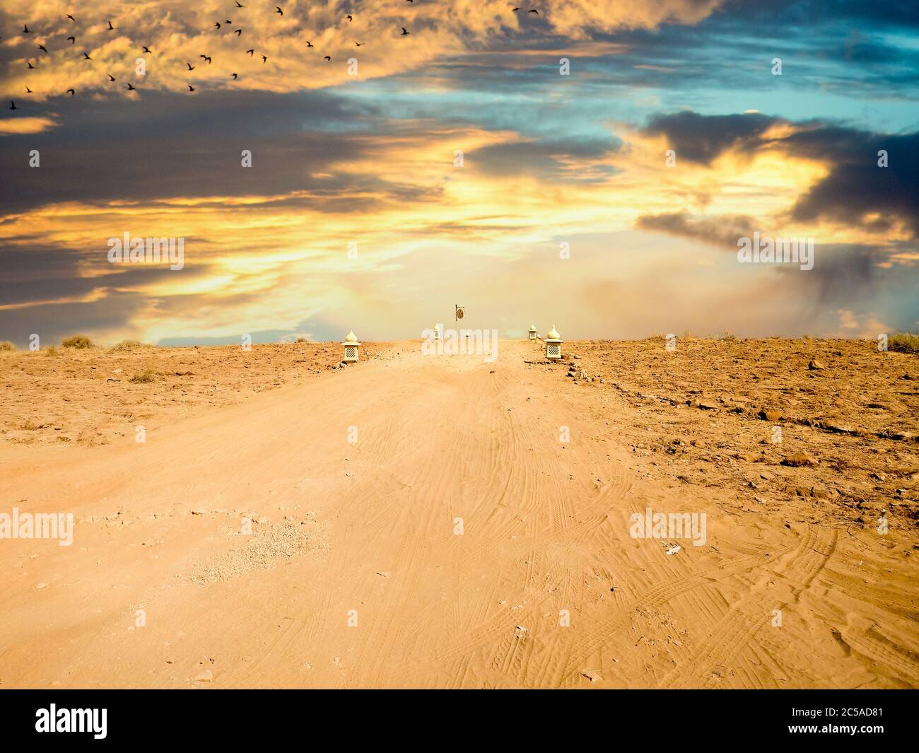 Empty dirt road with barren desert on both sides and blue sky above ...