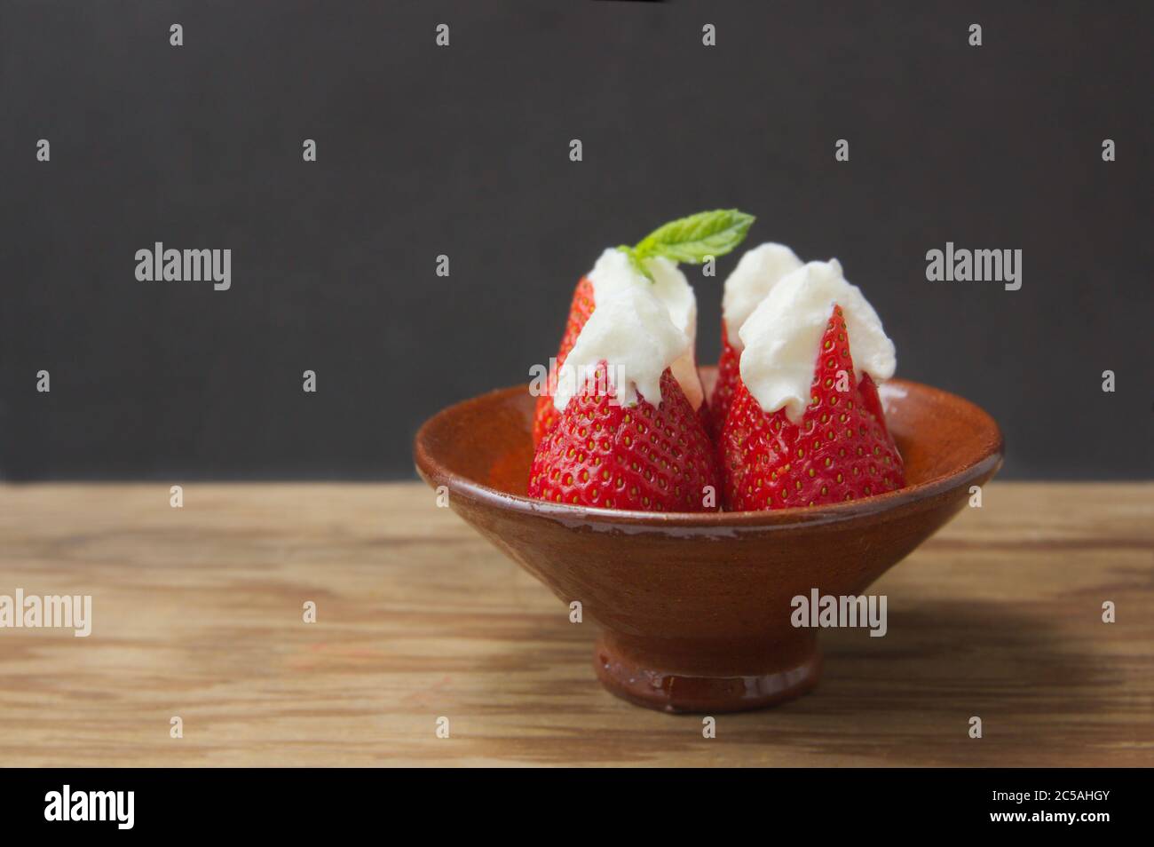 A serving of strawberries with cream on wooden table and dark ...
