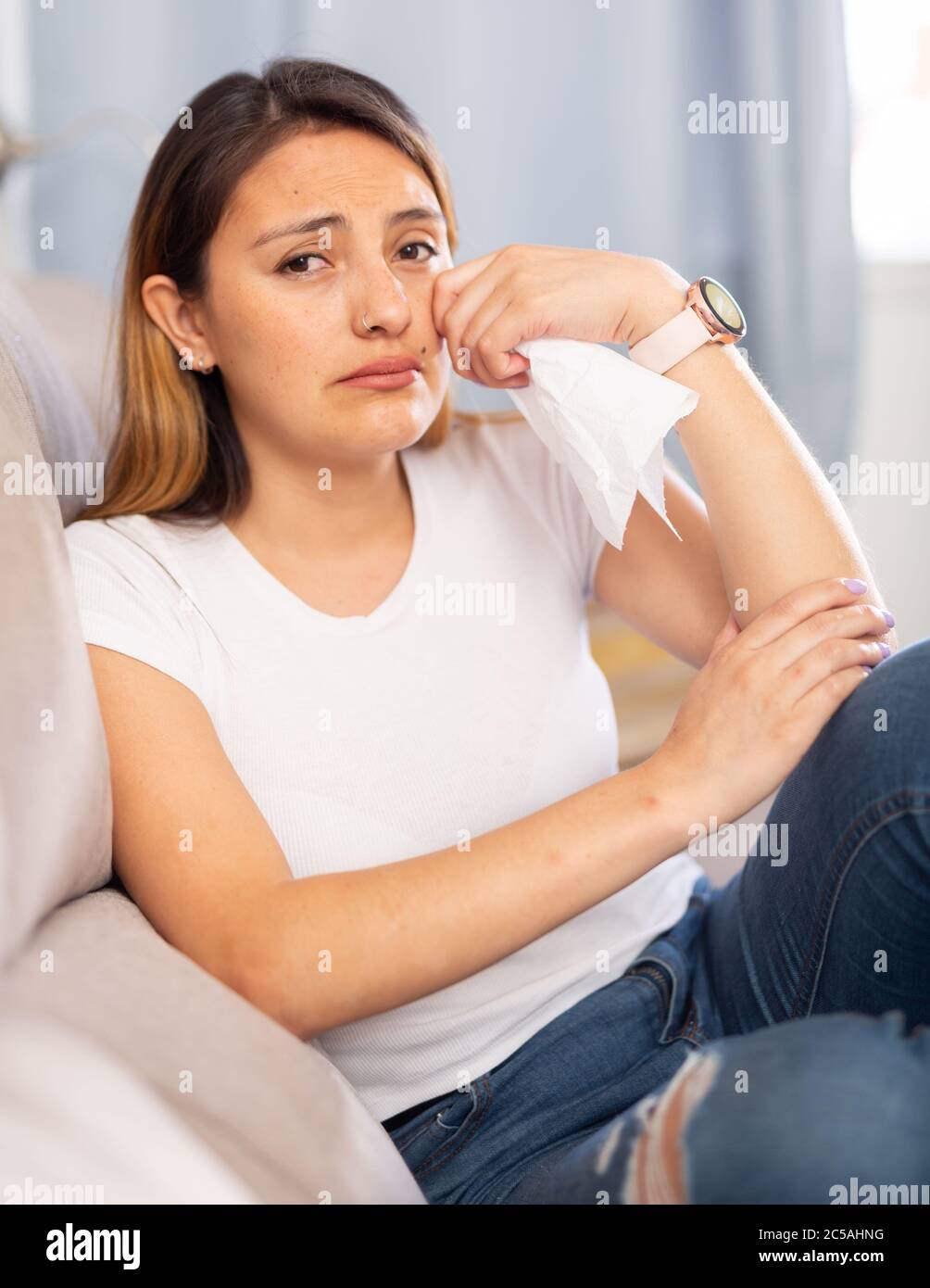 Upset latino woman crying while sitting on a sofa in a room Stock Photo ...