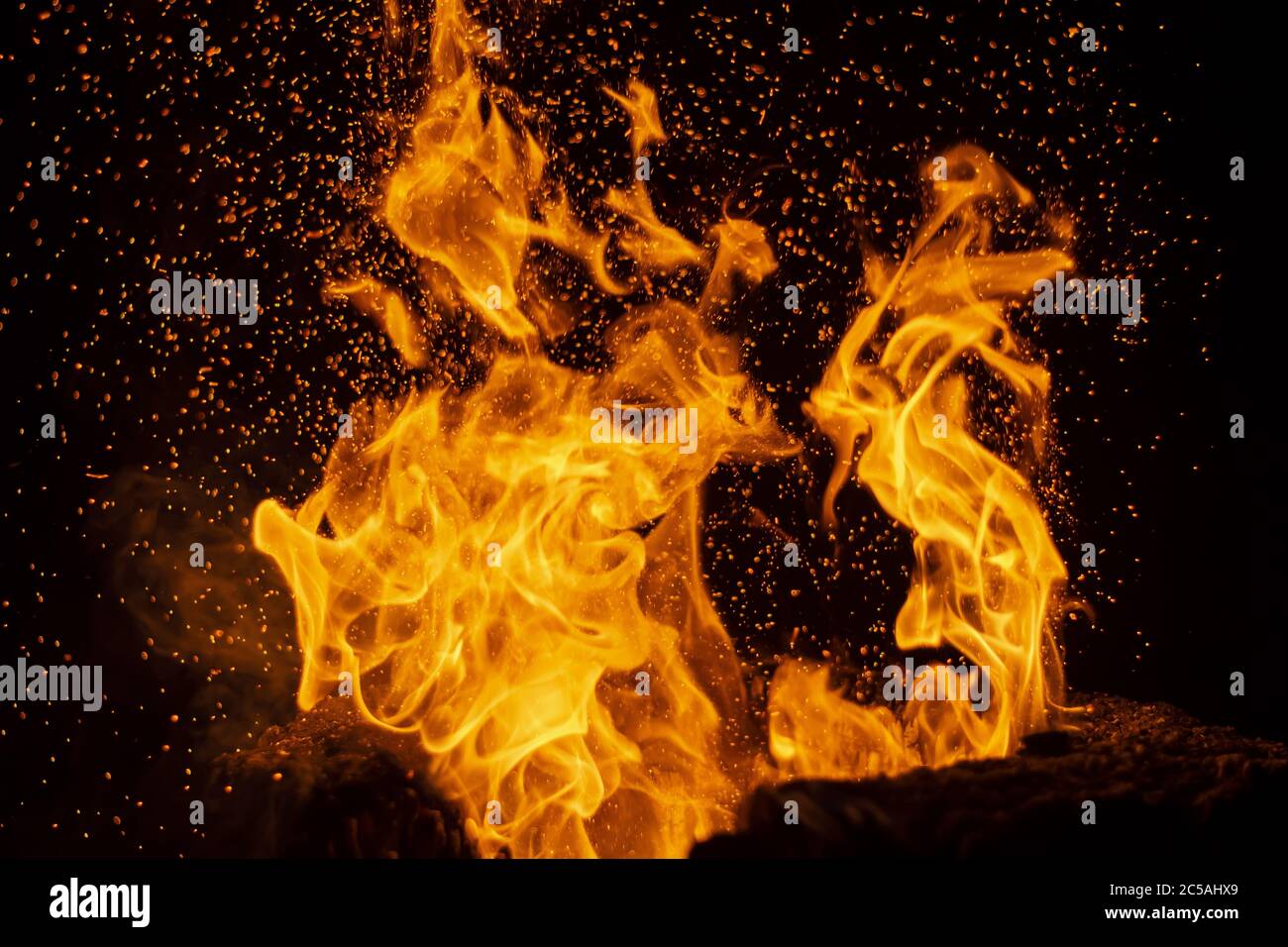 Closeup of a burning log with flying sparks creating a fiery background ...