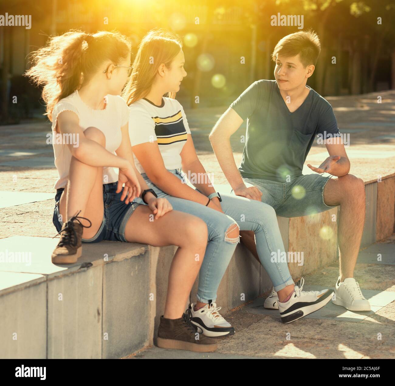 Group of modern teenagers hanging out on streets of city on warm summer ...