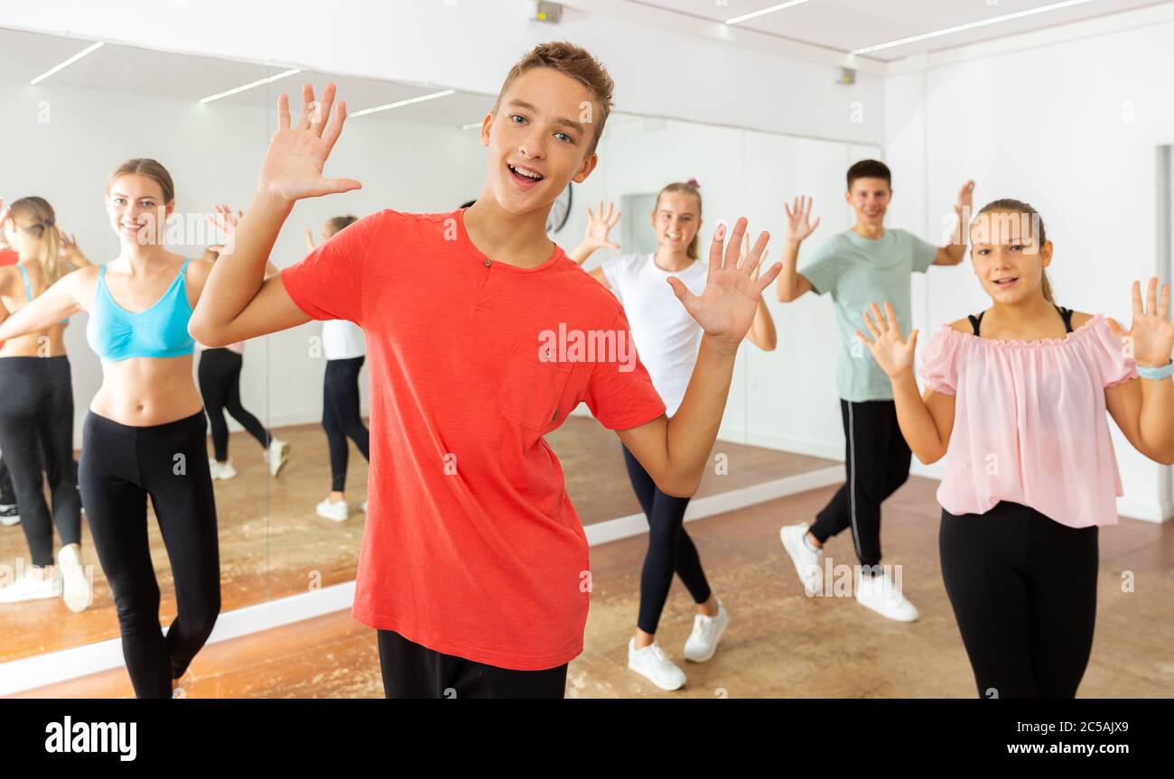 Portrait of cheerful teenage boy practicing dance movements with group ...