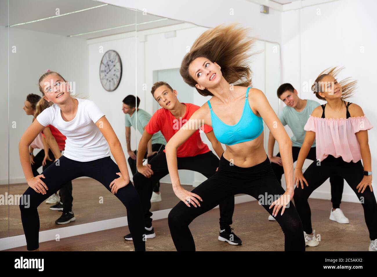 Cheerful teens practicing dance, stretching with young female trainer ...