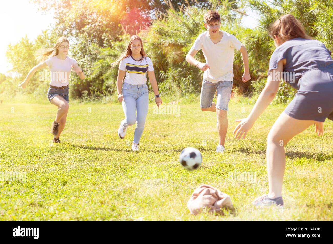 Company of glad teenagers playing football in park Stock Photo - Alamy