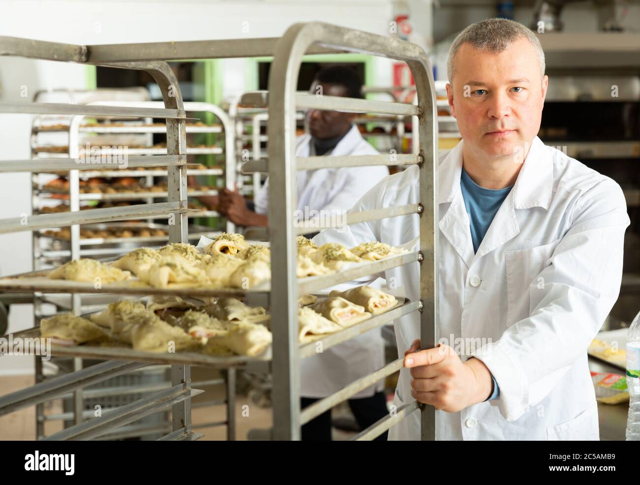 Experienced adult man working in bakery, pushing rack trolley with ...