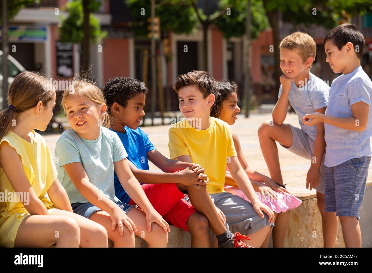 Group of positive children chatting together sitting at urban street ...