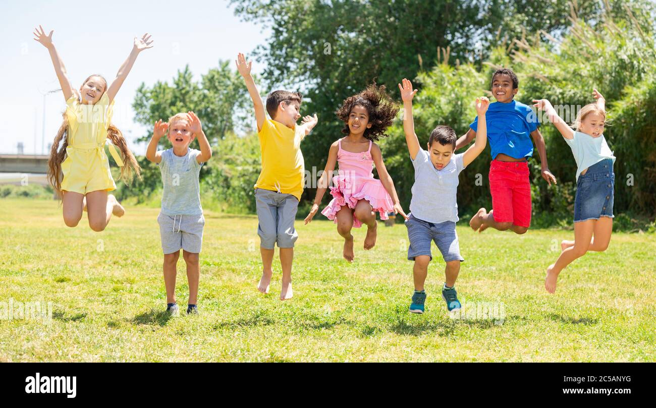 Group of happy schoolchildren jumping and smiling together in park ...