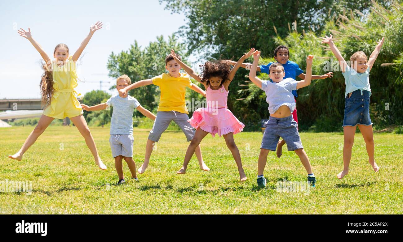 Happy school children jumping on the green lawn in summer park Stock ...