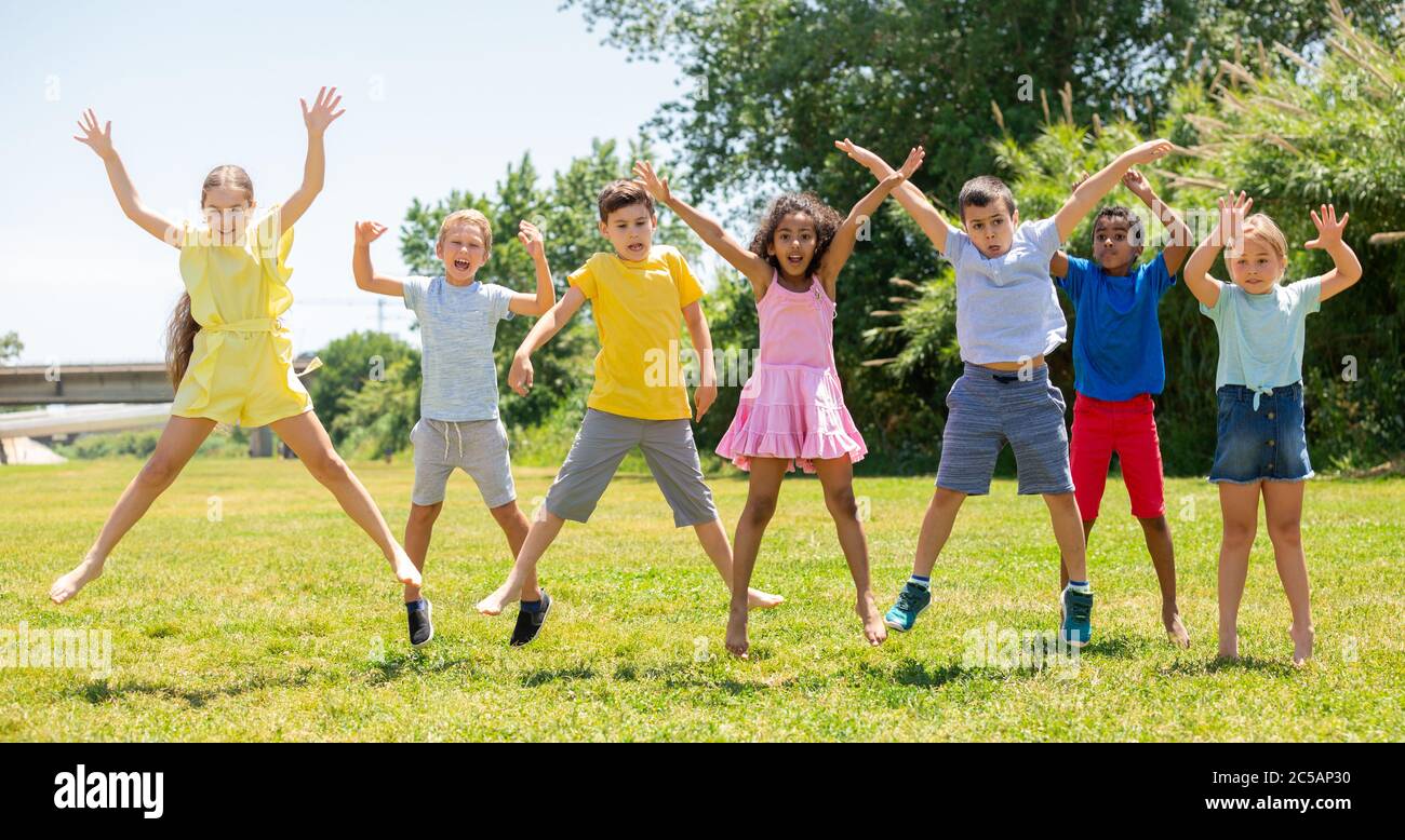 Happy school children jumping on the green lawn in summer park Stock ...