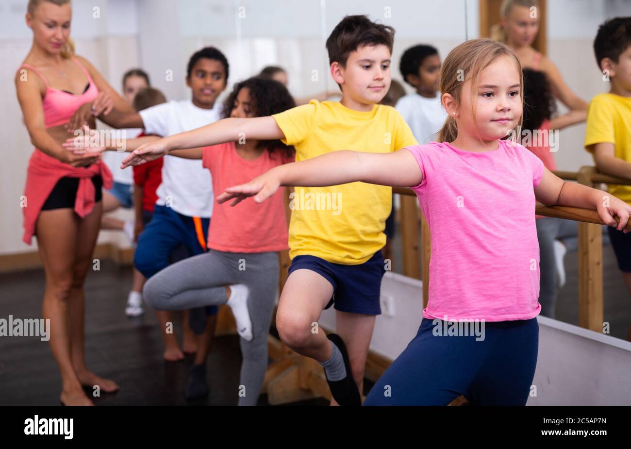 Focused children standing along ballet bar in dance studio during class ...