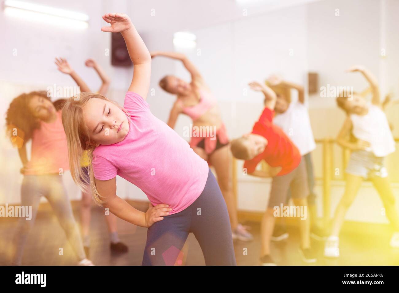 Portrait of little girl doing exercises during group class in dance ...