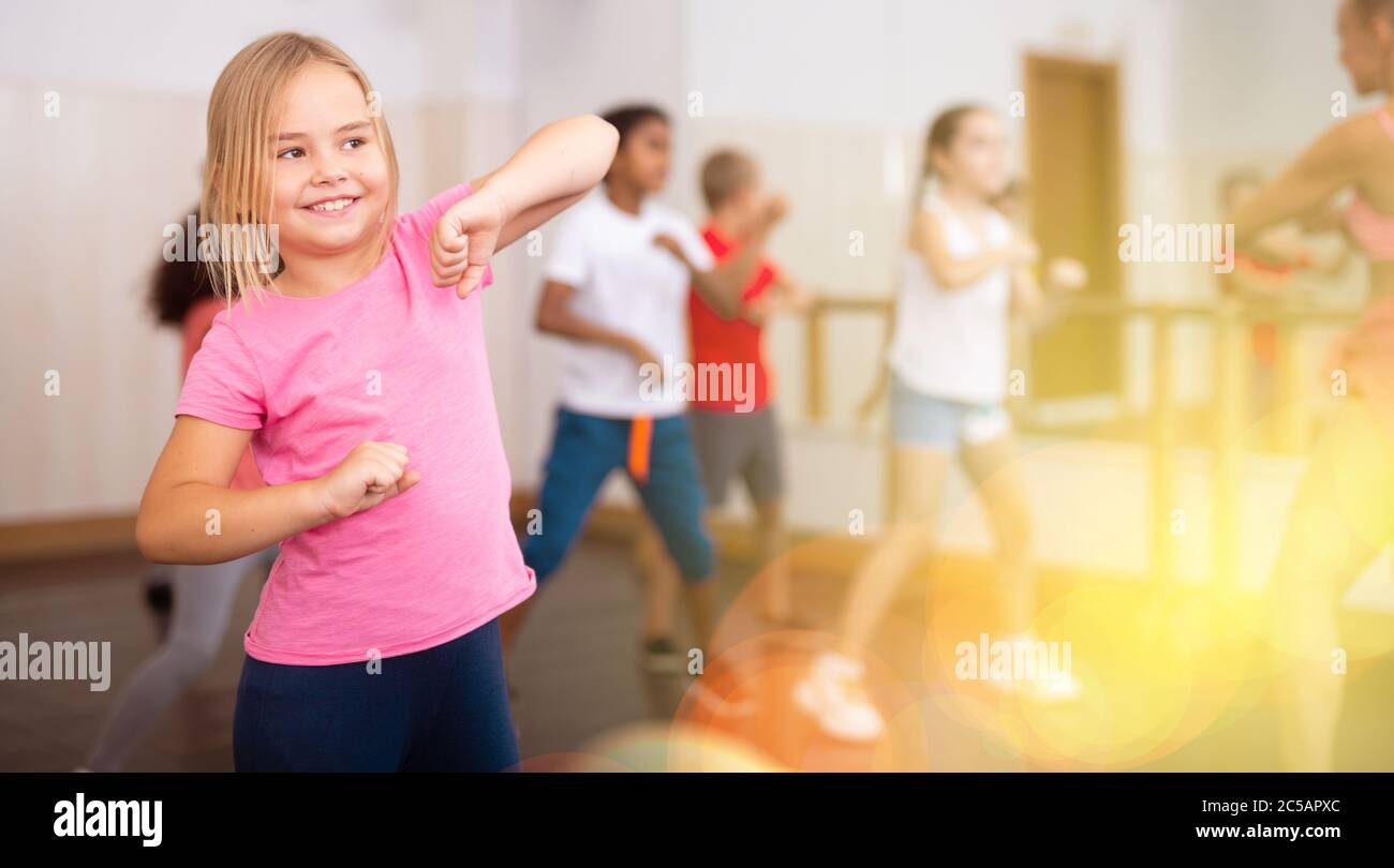 Positive girl exercising in group of classmates during dance class at ...