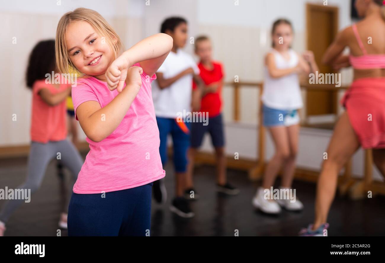 Positive girl exercising in group of classmates during dance class at ...