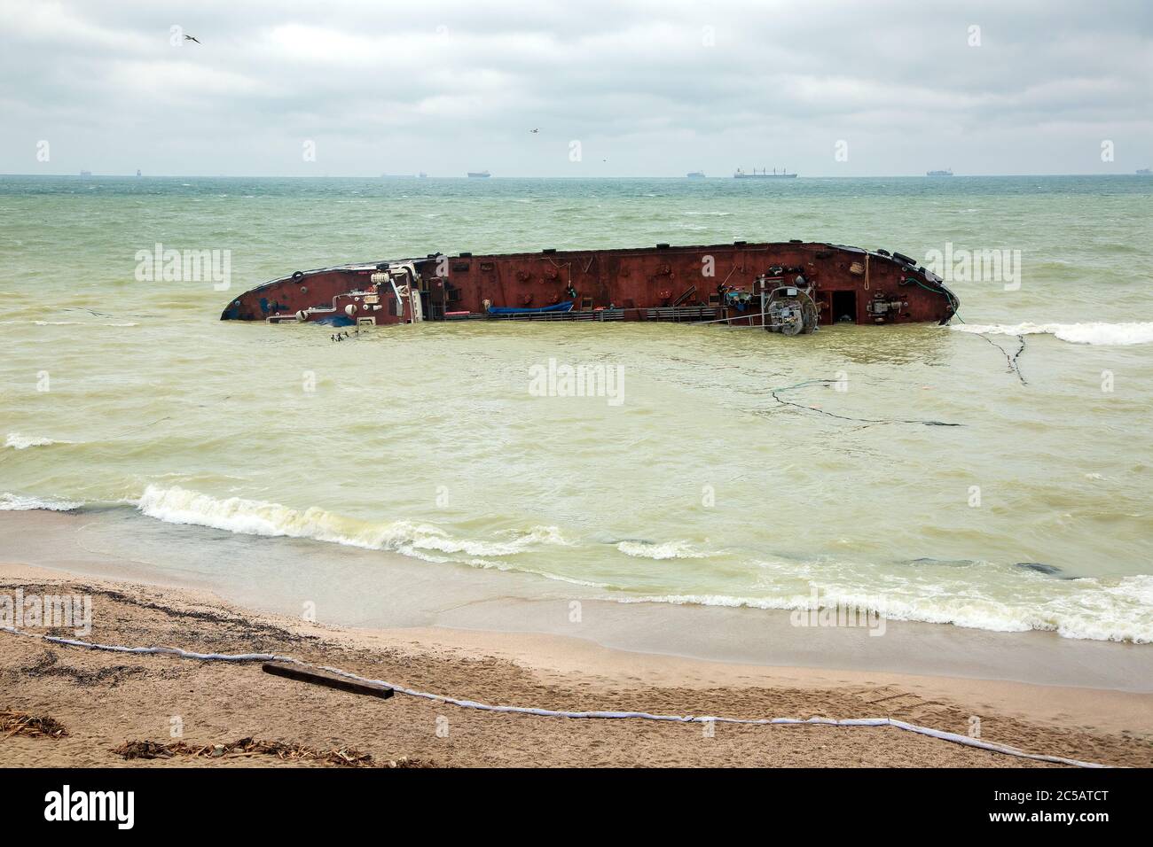 a cargo ship lies on its side, near the shore of a sandy beach with a ...