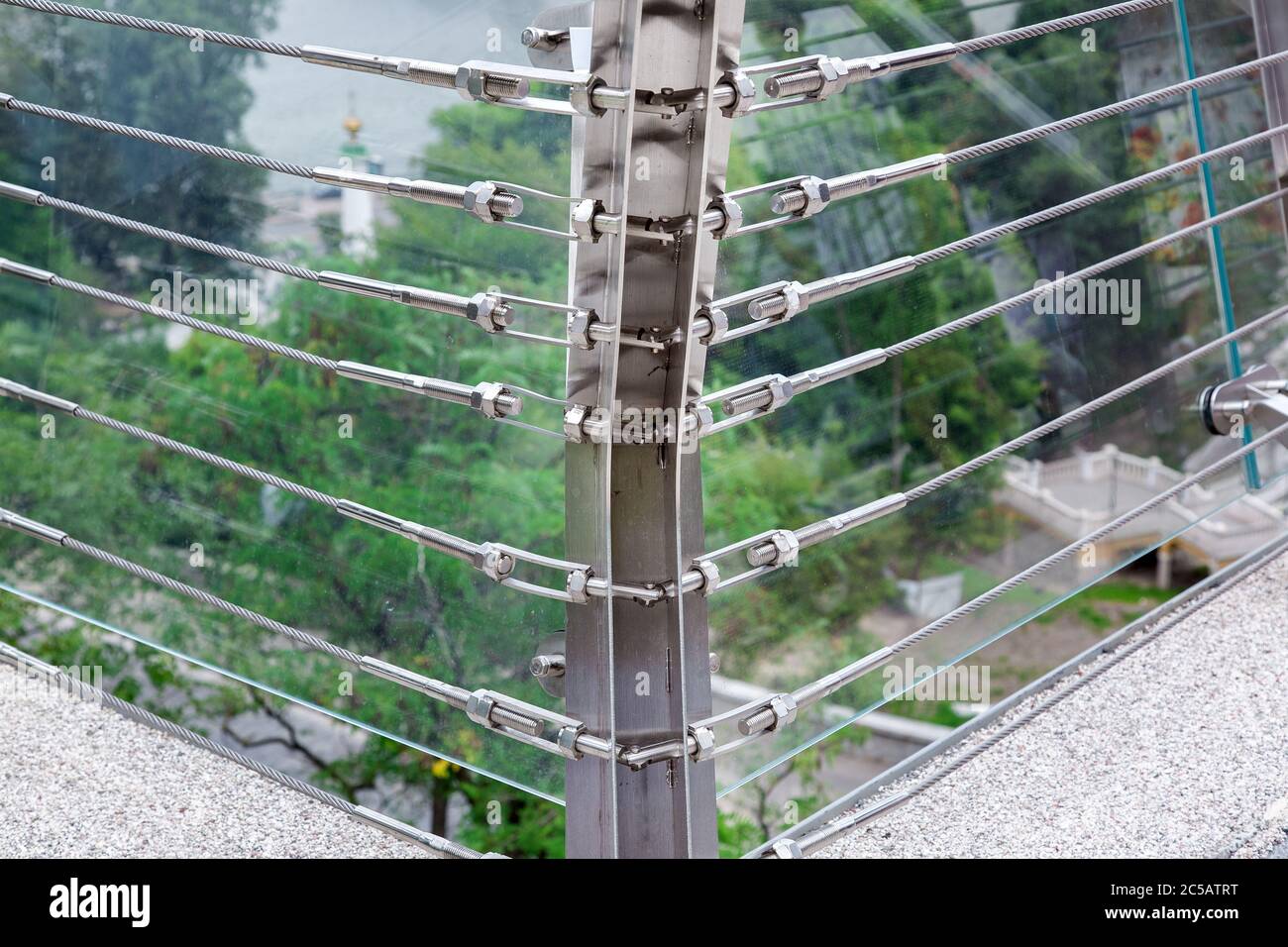 Corner of a glass bridge with tension steel cables over green trees ...
