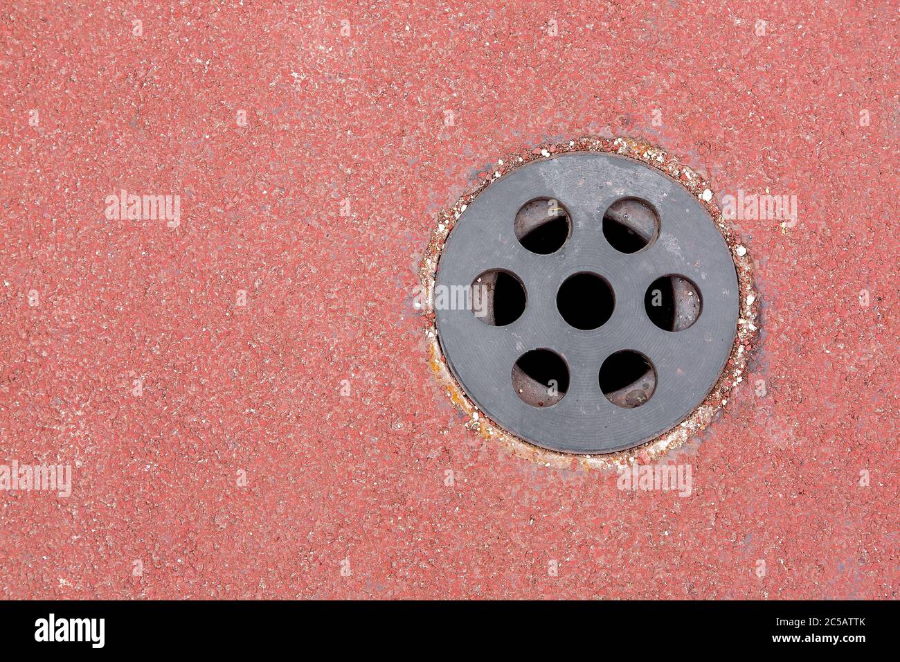 drainage hole with a round grid on a sports track made of red granular ...